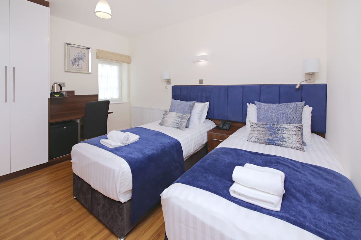 Quarto de hotel com duas camas, uma mesa e uma cadeira.