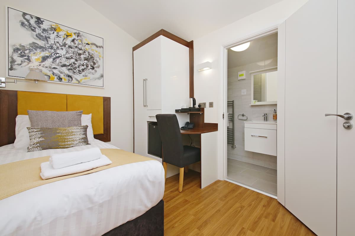 Quarto de hotel com cama, escrivaninha, cadeira, banheiro visível através de uma porta aberta e uma grande pintura abstrata na parede.