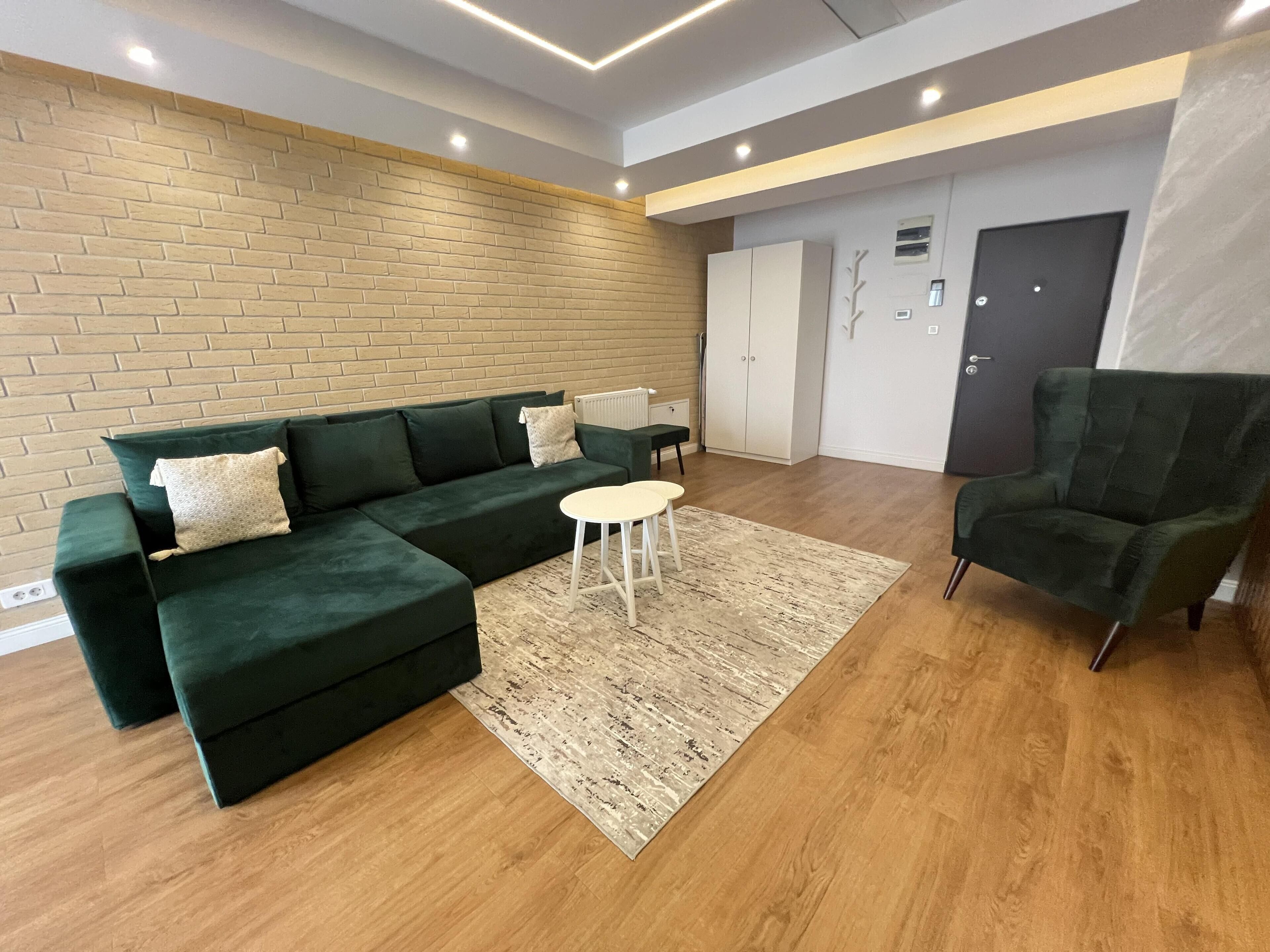 Uma sala de estar moderna com um sofá seccional, uma mesa redonda pequena e uma poltrona escura.