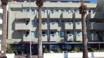 Um hotel com vários andares, varandas, palmeiras e um céu claro.
