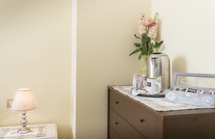 Uma secretária bem organizada com uma lâmpada, um vaso com flores, uma máquina de café e uma fotografia emoldurada.