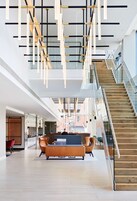Um lobby amplo com área de estar central, escadaria e design moderno com luminárias pendentes.