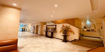 Um hall amplo com piso de mármore, escada e balcão de recepção com um vaso de flores.