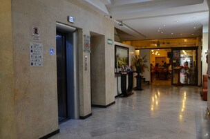Um saguão de hotel com piso de mármore, um elevador e uma mesa de recepção.