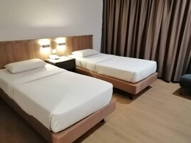 Quarto de hotel com duas camas de solteiro, cabeceira de madeira, luminárias de cabeceira e cortina.