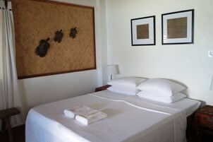 Cama bem arrumada com lençóis e toalhas brancos, cabeceira de madeira e parede com duas molduras.