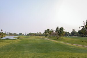 Um campo de golfe com lago, palmeiras e céu claro.