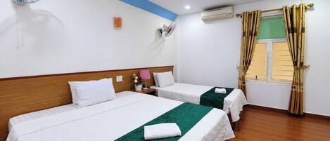Quarto de hotel com duas camas, cabeceira de madeira, ar condicionado fixado na parede, janela com cortinas e um ventilador de parede.