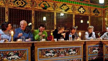 Um grupo de pessoas sentadas à mesa, com móveis decorados com entalhes coloridos e elaborados.
