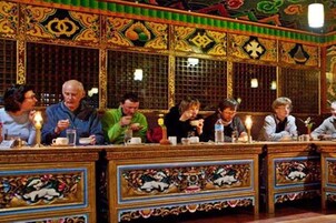 Um grupo de pessoas sentadas à mesa, com móveis decorados com entalhes coloridos e elaborados.