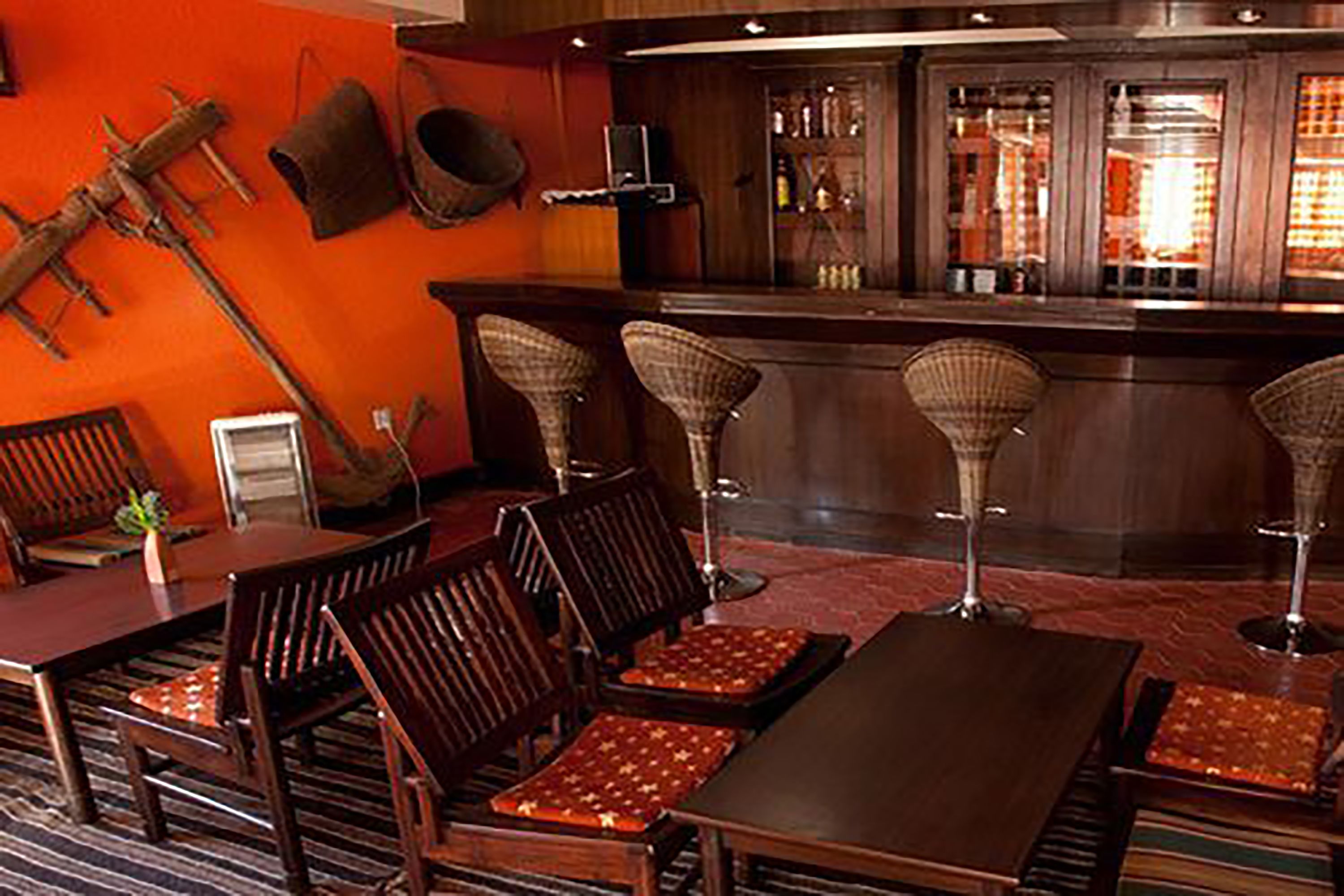 Uma área de bar com mobiliário de madeira, incluindo mesas e cadeiras, e um balcão com banquetas.
