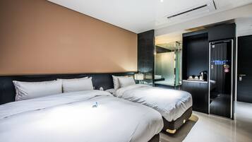 Quarto de hotel moderno com duas camas, um espelho grande, uma escrivaninha e um banheiro visível por uma porta de vidro.