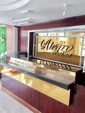 Uma receção com bancada de vidro e base de madeira, exibindo o nome 'Alegro Hotel' numa fonte decorativa.