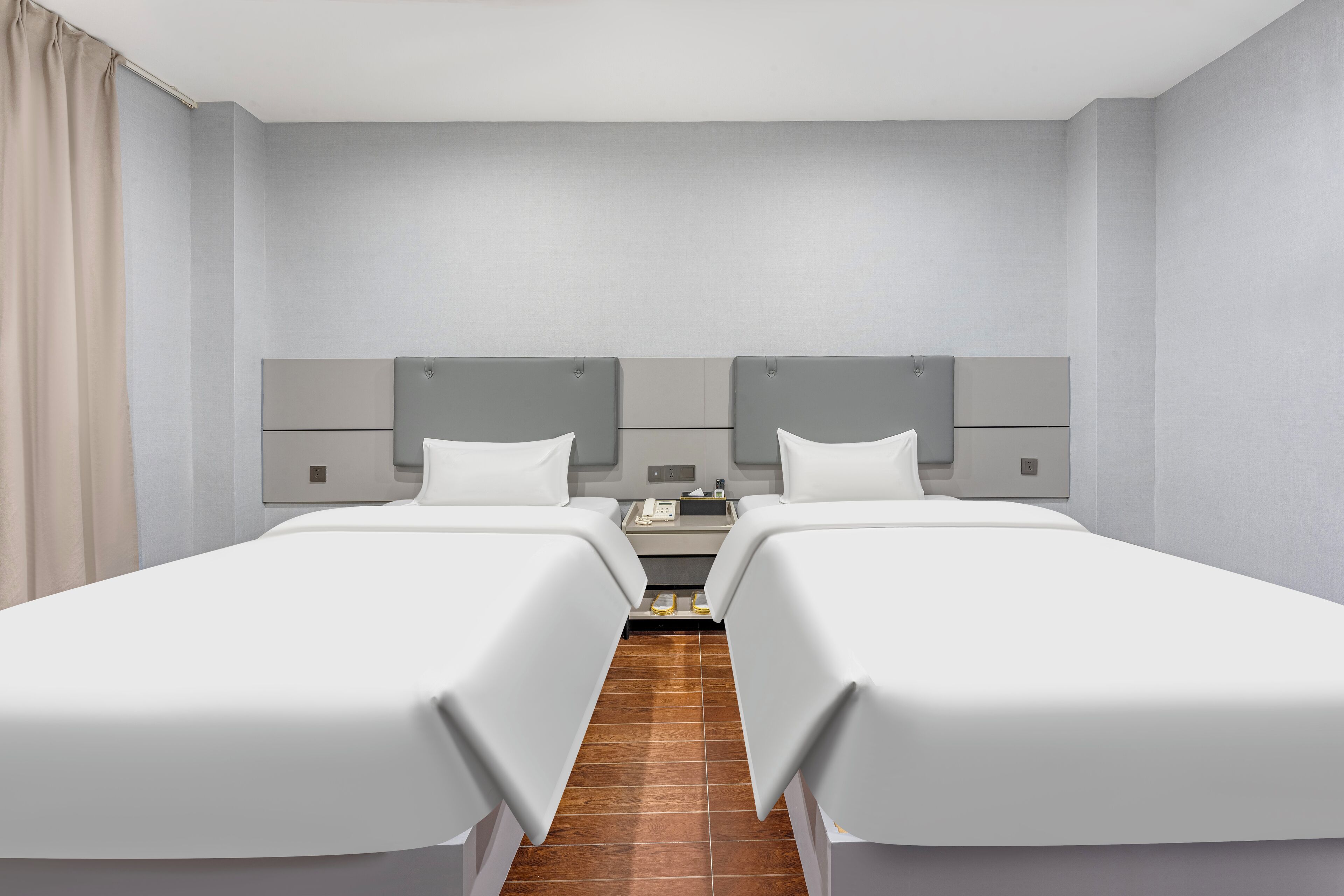 Quarto de hotel com duas camas de solteiro, mesa de cabeceira, abajur e uma pequena mesa.