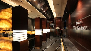Um hall de hotel moderno com uma recepção central, uma escadaria e uma parede com o nome do hotel.