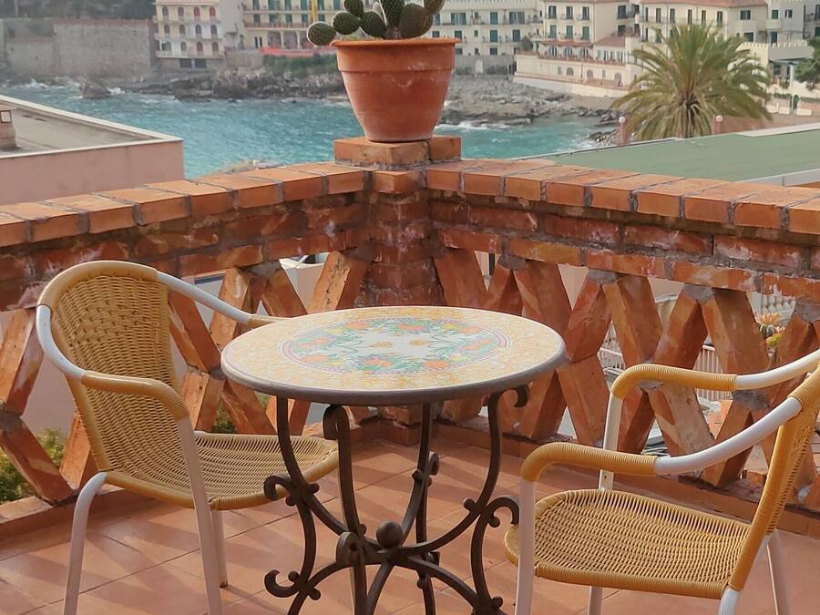 Terraço com mesa e cadeiras de vime, com vista para a área costeira, edifícios e uma colina.