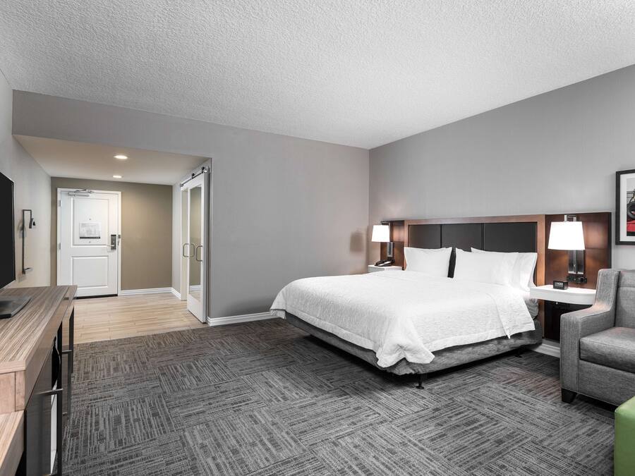 Quarto de hotel com cama, escrivaninha, televisão, cadeira e abajur.