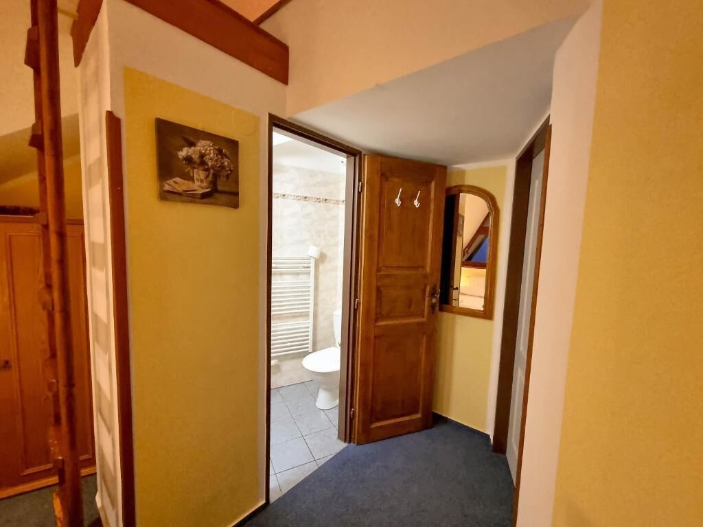 Corredor com porta de madeira, um pequeno quadro na parede e vista para um banheiro com vaso sanitário e chuveiro.