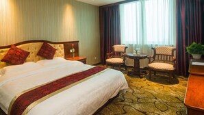 Quarto de hotel com uma cama grande, duas poltronas, uma mesinha e um vaso de plantas.