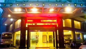 Entrada de hotel com um letreiro de neon, porta de vidro e uma van estacionada.