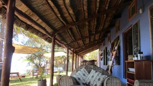 Uma área de estar coberta ao ar livre, com mesa, cadeiras e telhado de palha.