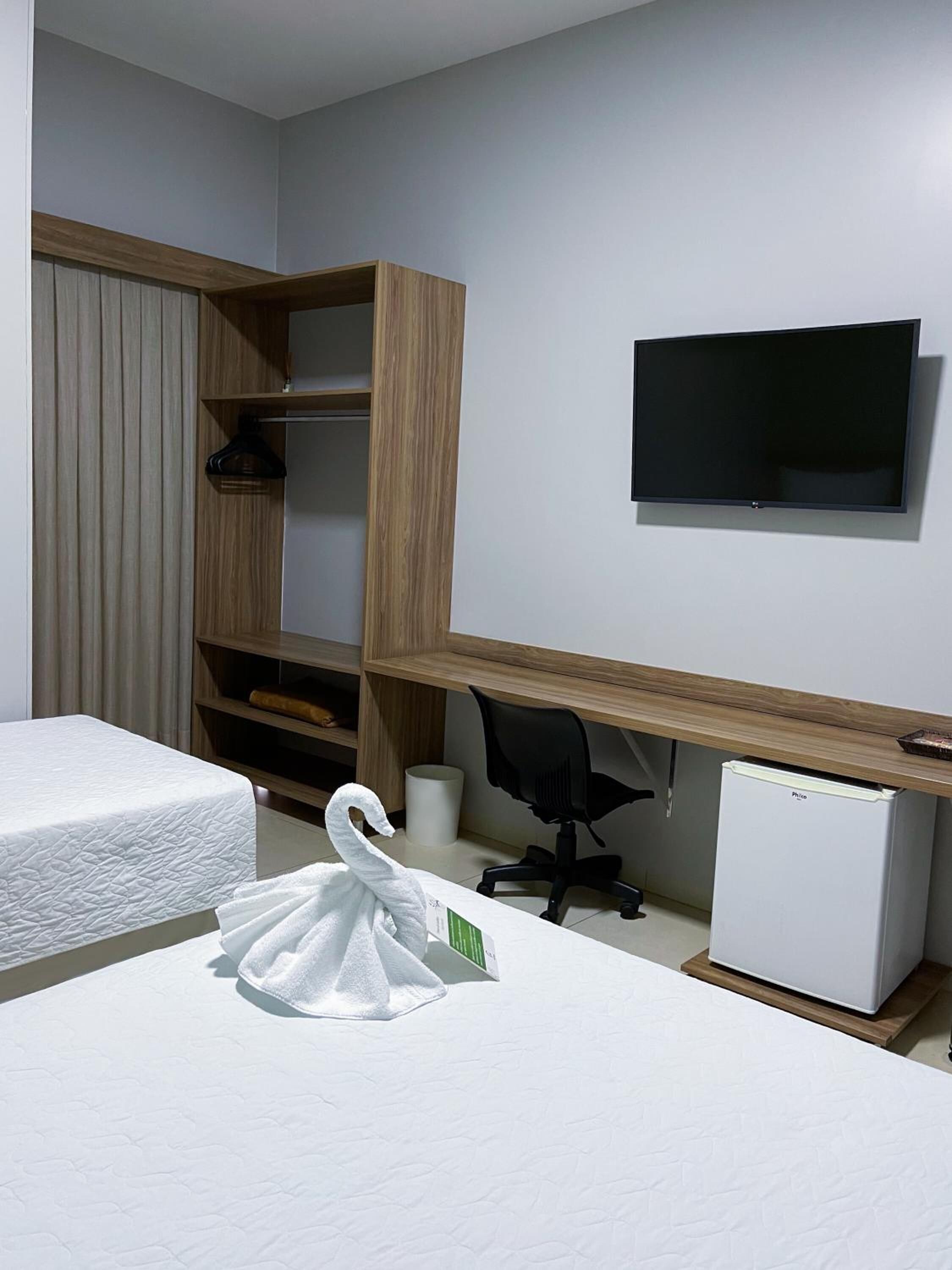 Quarto com cama, escrivaninha, cadeira, televisão e minibar.