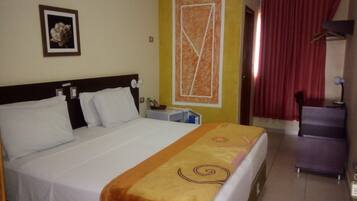 Quarto de hotel com uma cama, mesa de cabeceira, escrivaninha e cortina vermelha.