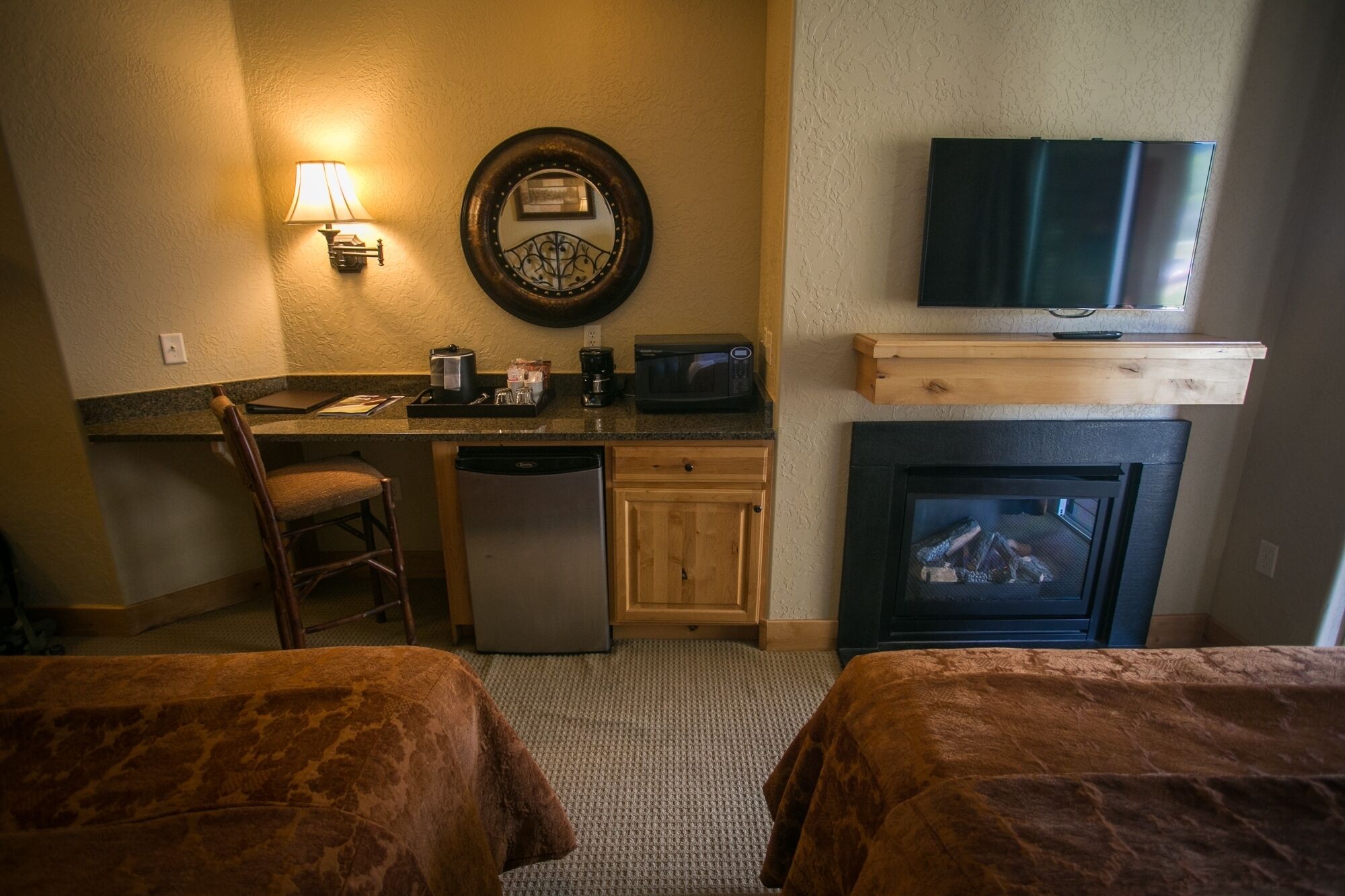 Quarto de hotel com cozinha compacta, lareira, televisão e duas camas.