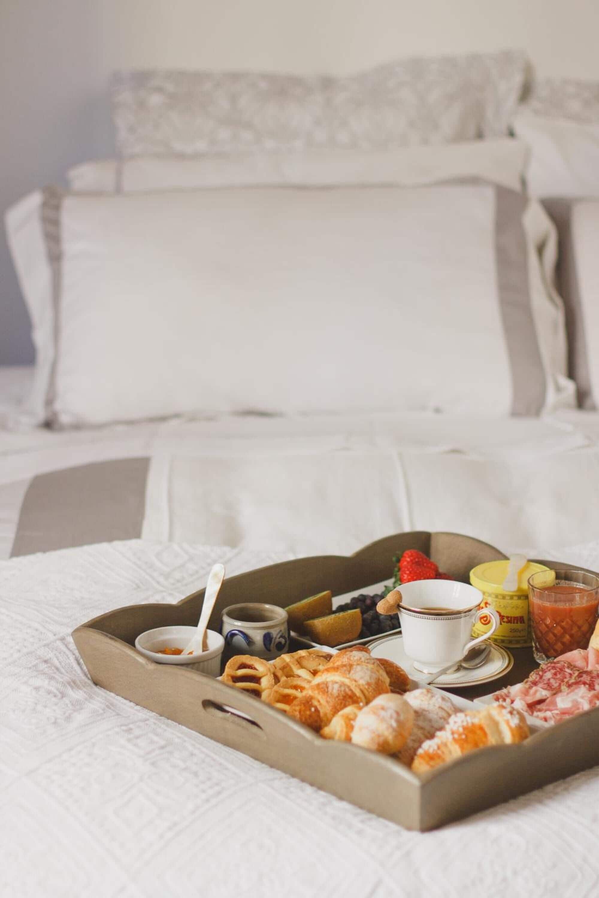 Uma bandeja de café da manhã com doces, frutas e bebidas sobre a cama.