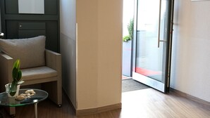 Um hall de hotel moderno, com área de estar, porta de vidro que dá para o exterior e uma pequena mesa com uma planta.