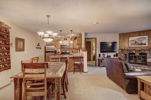 Uma sala de estar ampla com lareira, um espaço de refeições com mobiliário de madeira e uma cozinha com eletrodomésticos modernos.