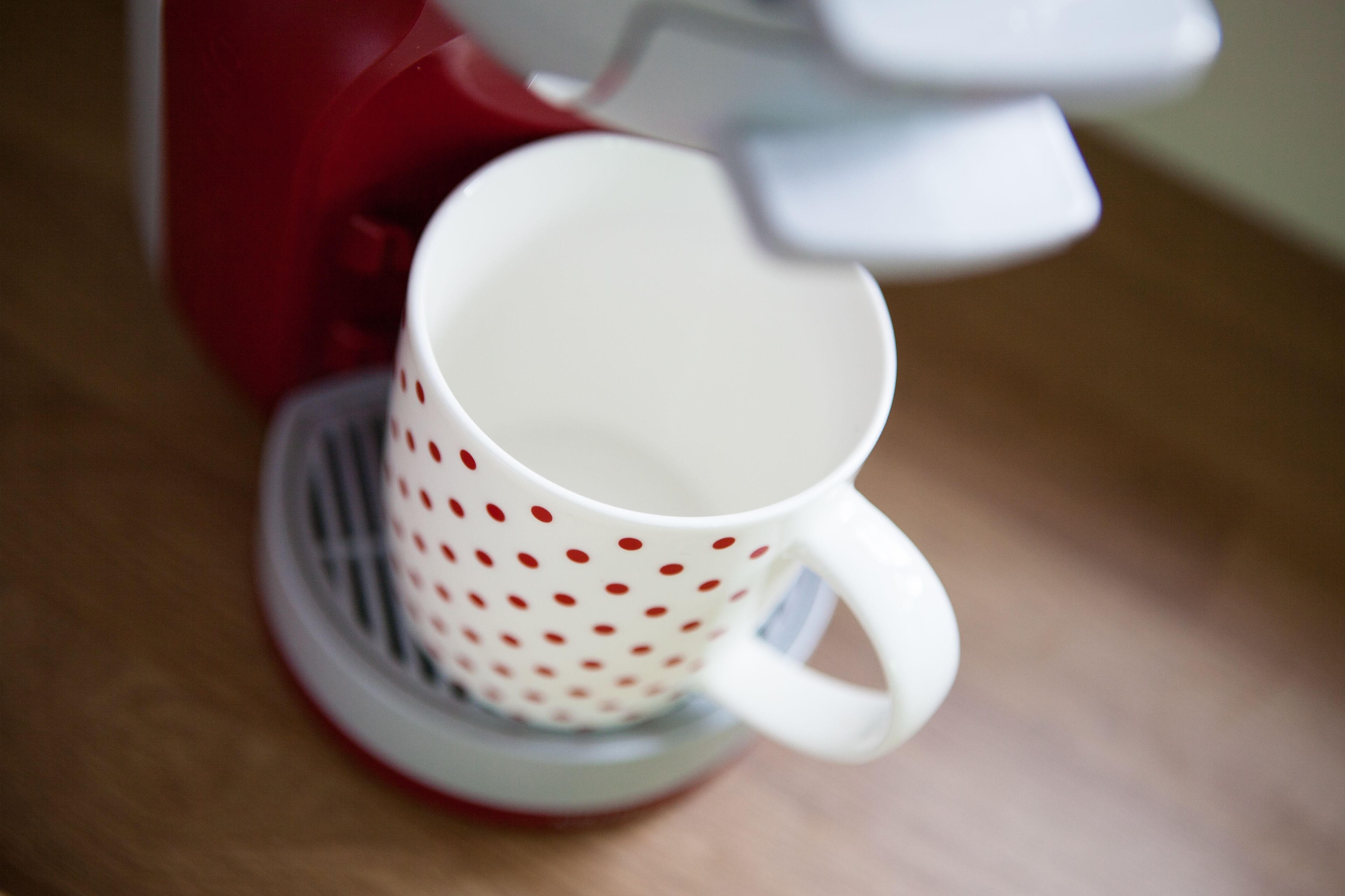 Uma caneca branca com bolinhas vermelhas sobre um apoio para copos.
