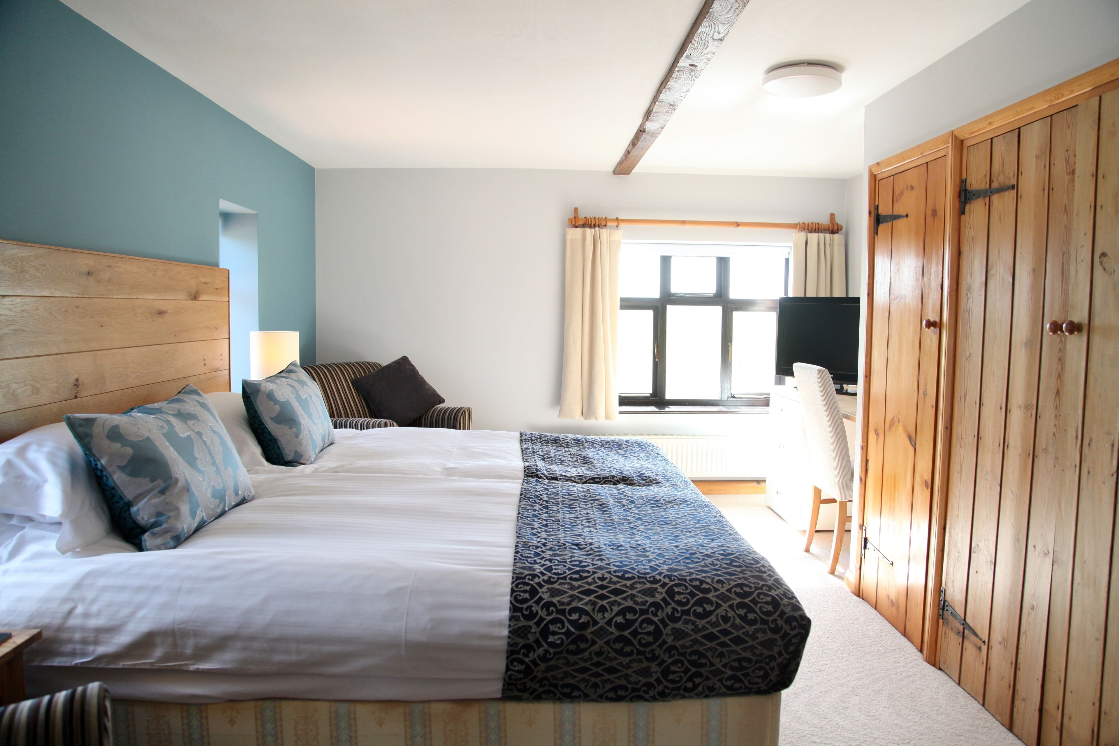 Quarto com cama grande, guarda-roupa de madeira, televisão e janela com cortinas.