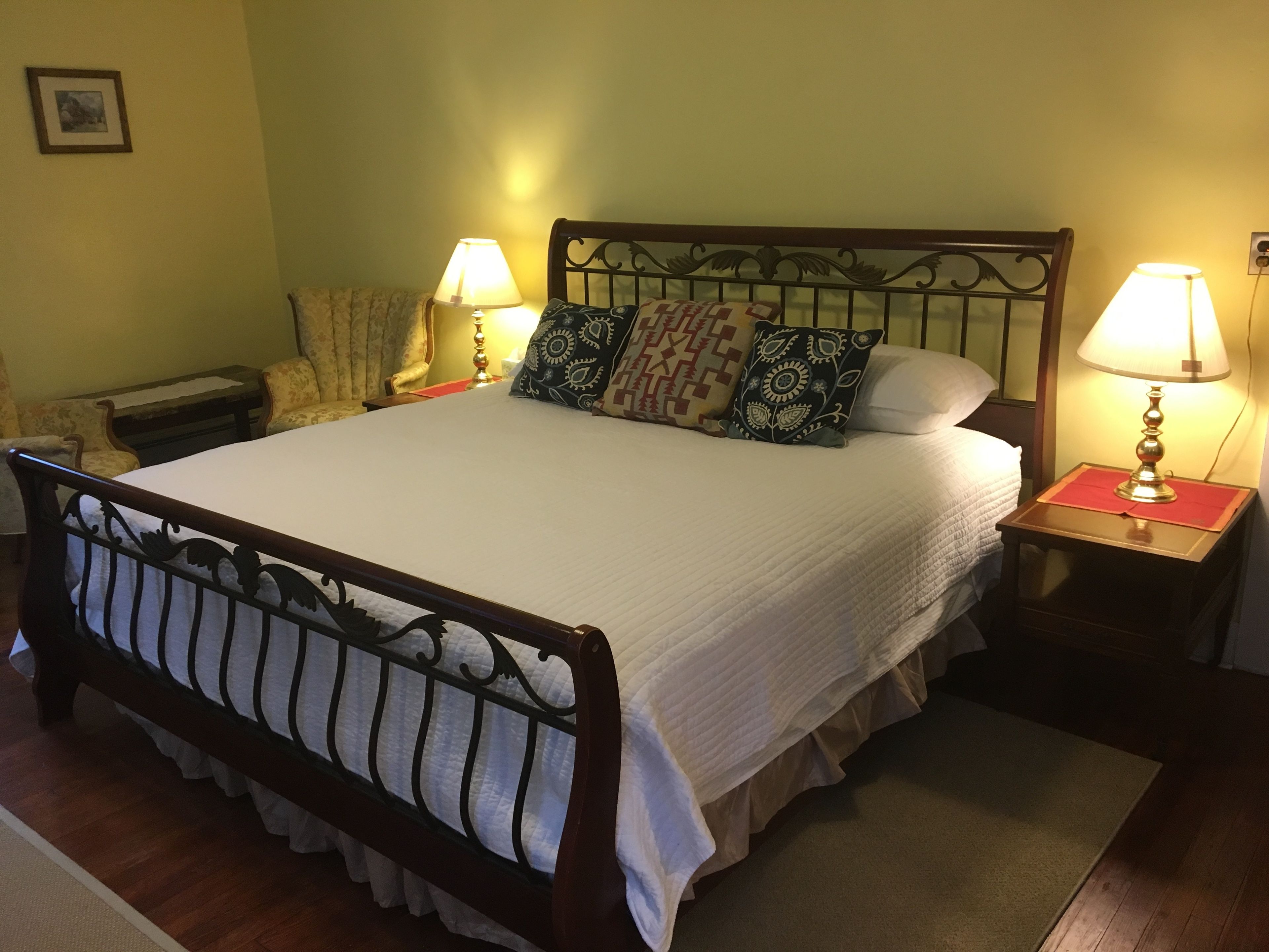 Cama bem arrumada com cabeceira de madeira, duas luminárias laterais e almofadas estampadas.