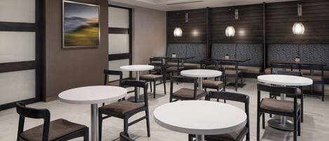 Um restaurante moderno com mesas e cadeiras redondas, um quadro grande na parede e iluminação pendente.