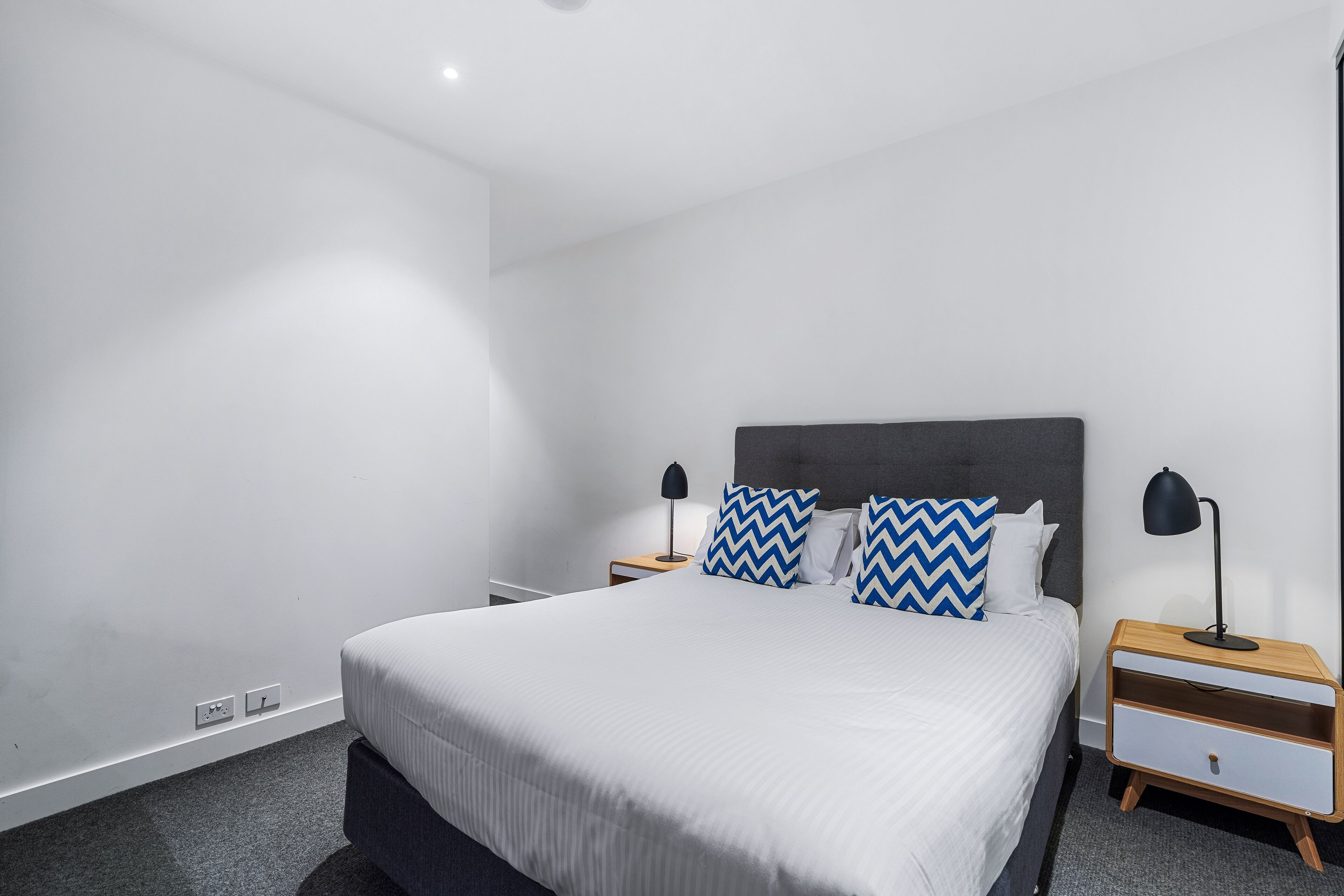 Quarto de hotel moderno com uma cama grande, duas mesas de cabeceira e um criado-mudo.