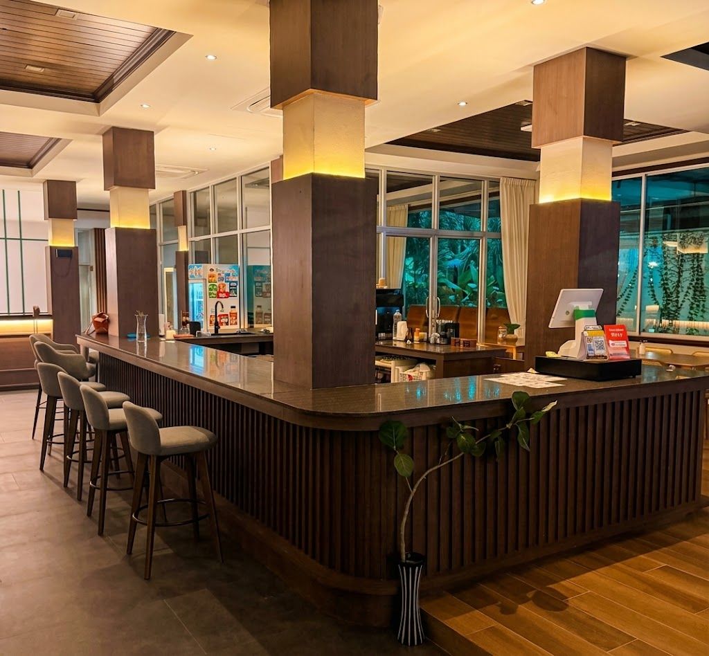 Uma área de recepção de hotel com um balcão curvo, banquetas e vista para o exterior.