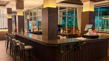 Uma área de recepção de hotel com um balcão curvo, banquetas e vista para o exterior.