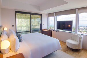 Quarto de hotel moderno com uma cama grande, uma escrivaninha, uma cadeira e uma televisão.