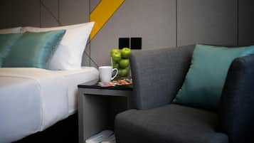 Quarto de hotel moderno com uma cama, uma mesinha com uma revista, uma chávena e uma taça de maçãs.