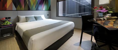 Quarto de hotel moderno com uma cama grande, uma escrivaninha com cadeira, uma janela com vista para a cidade e um design de parede colorido.