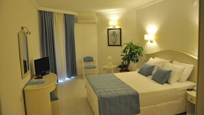 Quarto de hotel com cama, mesa de cabeceira, cadeira, escrivaninha com um computador e um vaso de planta.