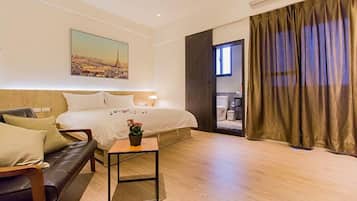 Quarto de hotel moderno com uma cama, uma mesinha com uma planta, um sofá e um quadro na parede.