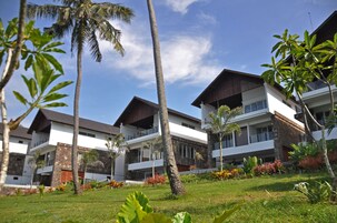 Um hotel moderno com vários andares, grandes janelas e um jardim bem cuidado com palmeiras e plantas coloridas.