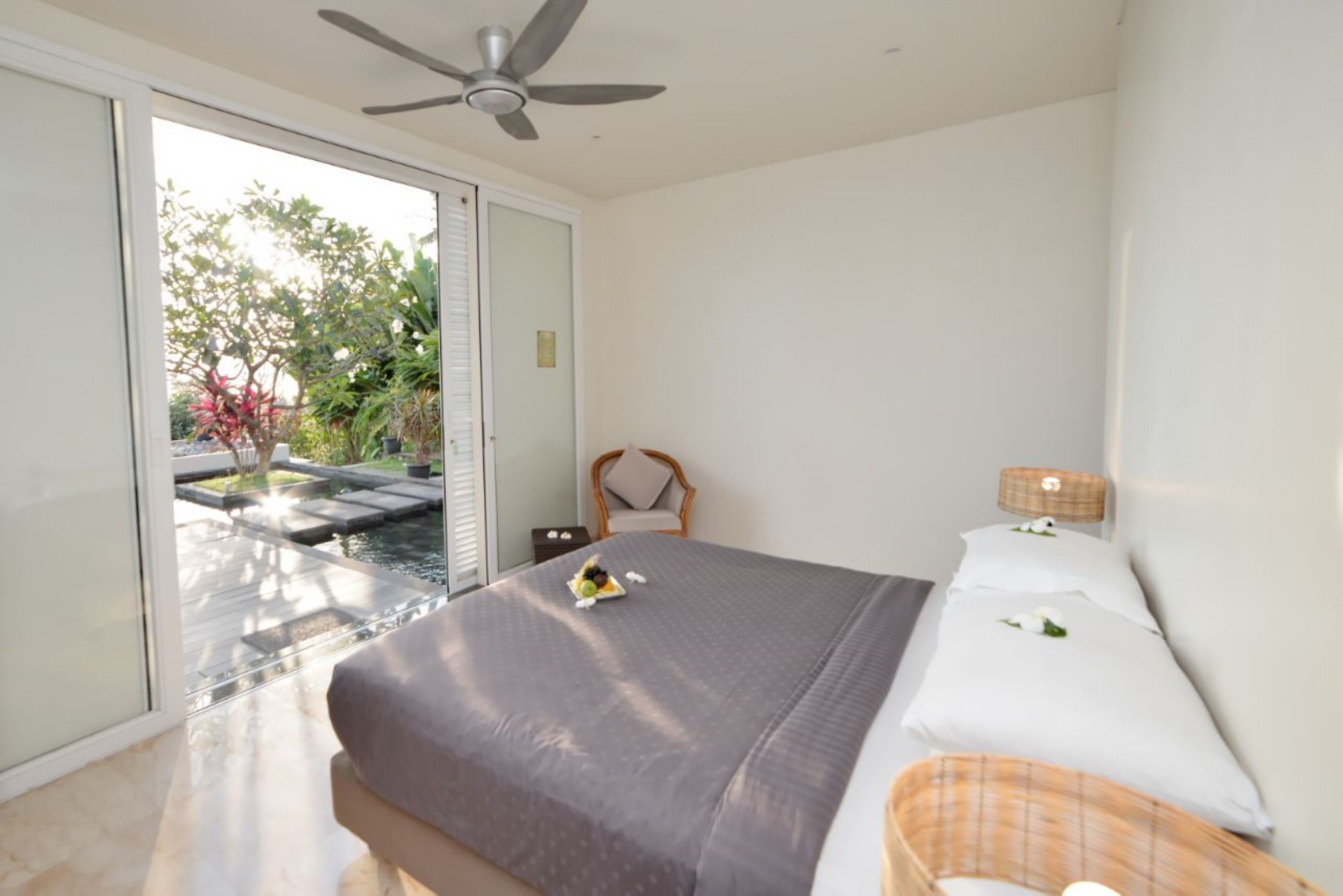 Quarto com cama, mesa de cabeceira, cadeira e vista para um jardim com lago.