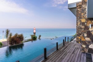 Um deck de madeira com vista para um mar azul e límpido, com um farol ao longe.