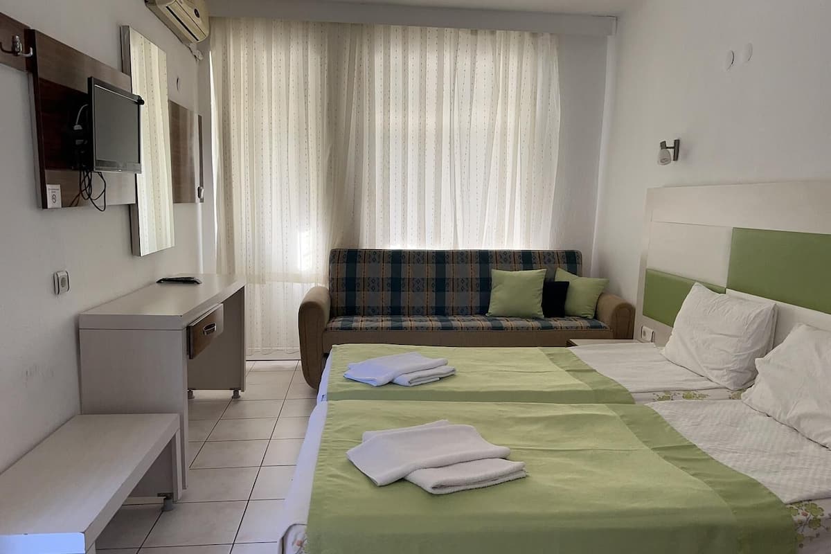 Quarto de hotel com cama, sofá, escrivaninha e televisão.