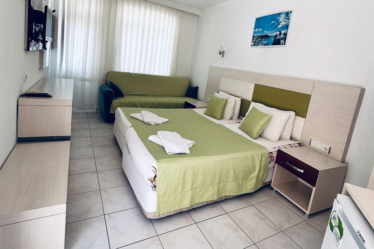 Quarto de hotel com cama, escrivaninha, cadeira, guarda-roupa e banheiro.