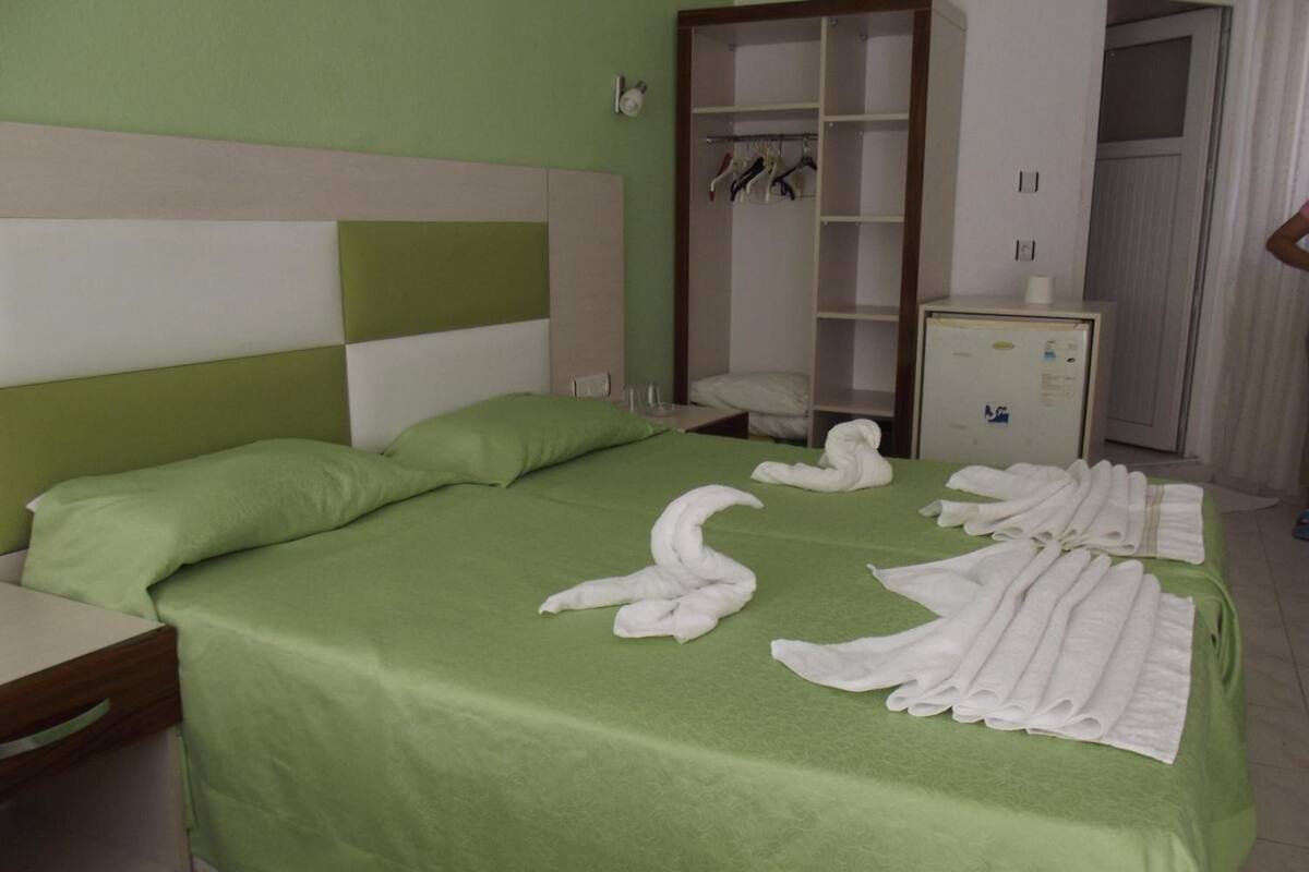 Quarto de hotel com cama, guarda-roupa, escrivaninha e pequeno armário.