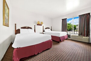Quarto de hotel com duas camas, uma janela grande com cortinas, um tapete estampado e um quadro na parede.